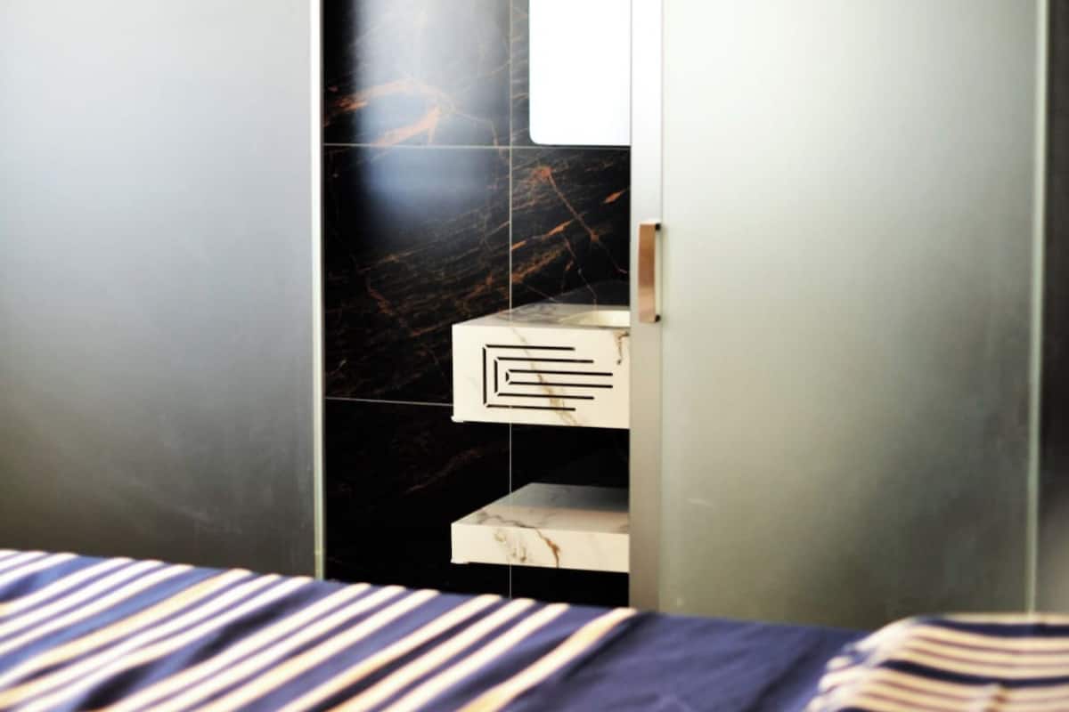 Quarto moderno com cama, mesa de cabeceira e espelho.