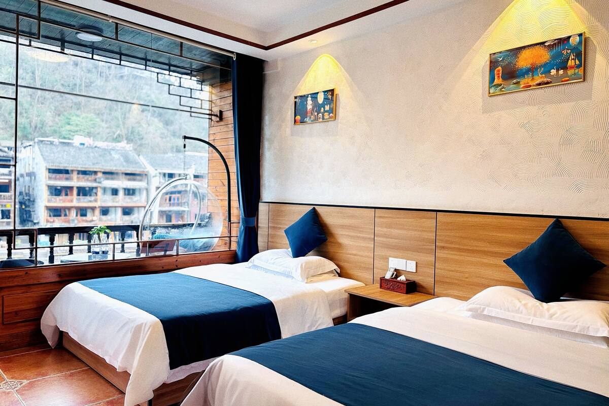 Quarto de hotel com duas camas, uma janela ampla com vista para edifícios e arte decorativa na parede.