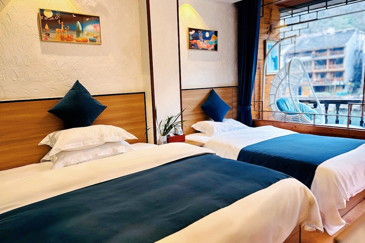 Quarto de hotel com duas camas, vista para a cidade pela janela e obras de arte nas paredes.