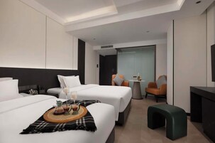 Quarto de hotel moderno com duas camas, uma pequena área de estar e uma televisão.