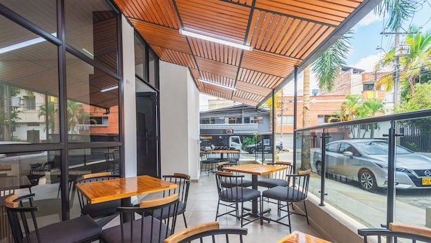 Um restaurante com mesas e cadeiras de madeira, grandes janelas e vista para a rua.