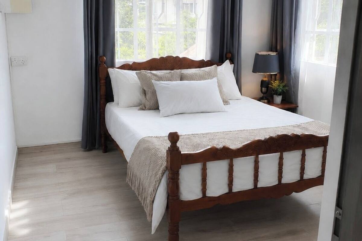 Quarto com cama de madeira, mesa de cabeceira com luminária e vista para o verde lá fora.