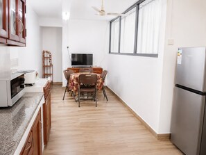 Uma cozinha compacta com mesa, cadeiras, geladeira e televisão.