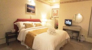 Quarto de hotel com cama, escrivaninha, televisão e mesa de cabeceira.