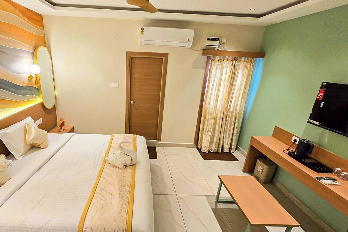 Quarto de hotel com cama, escrivaninha, televisão, aparelho de ar condicionado e cortina.