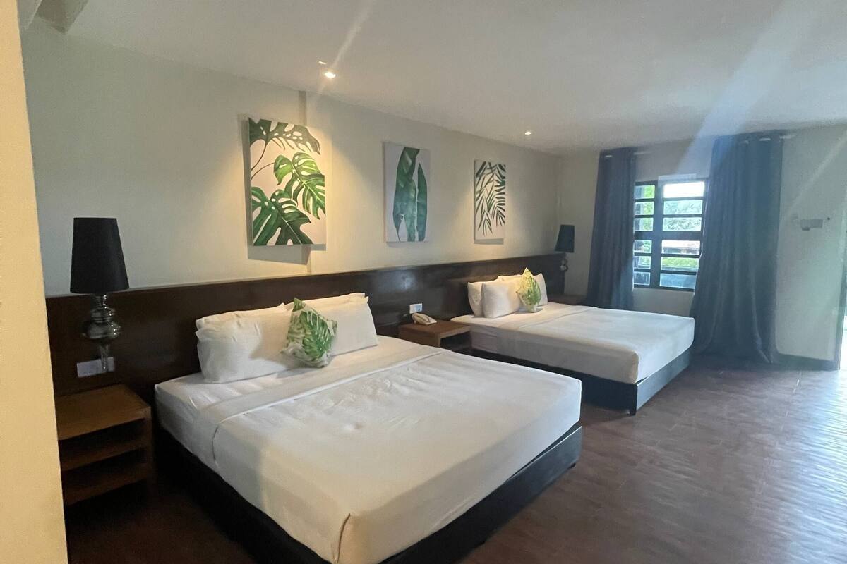 Quarto de hotel com duas camas, uma mesa de cabeceira, uma luminária e obras de arte nas paredes.