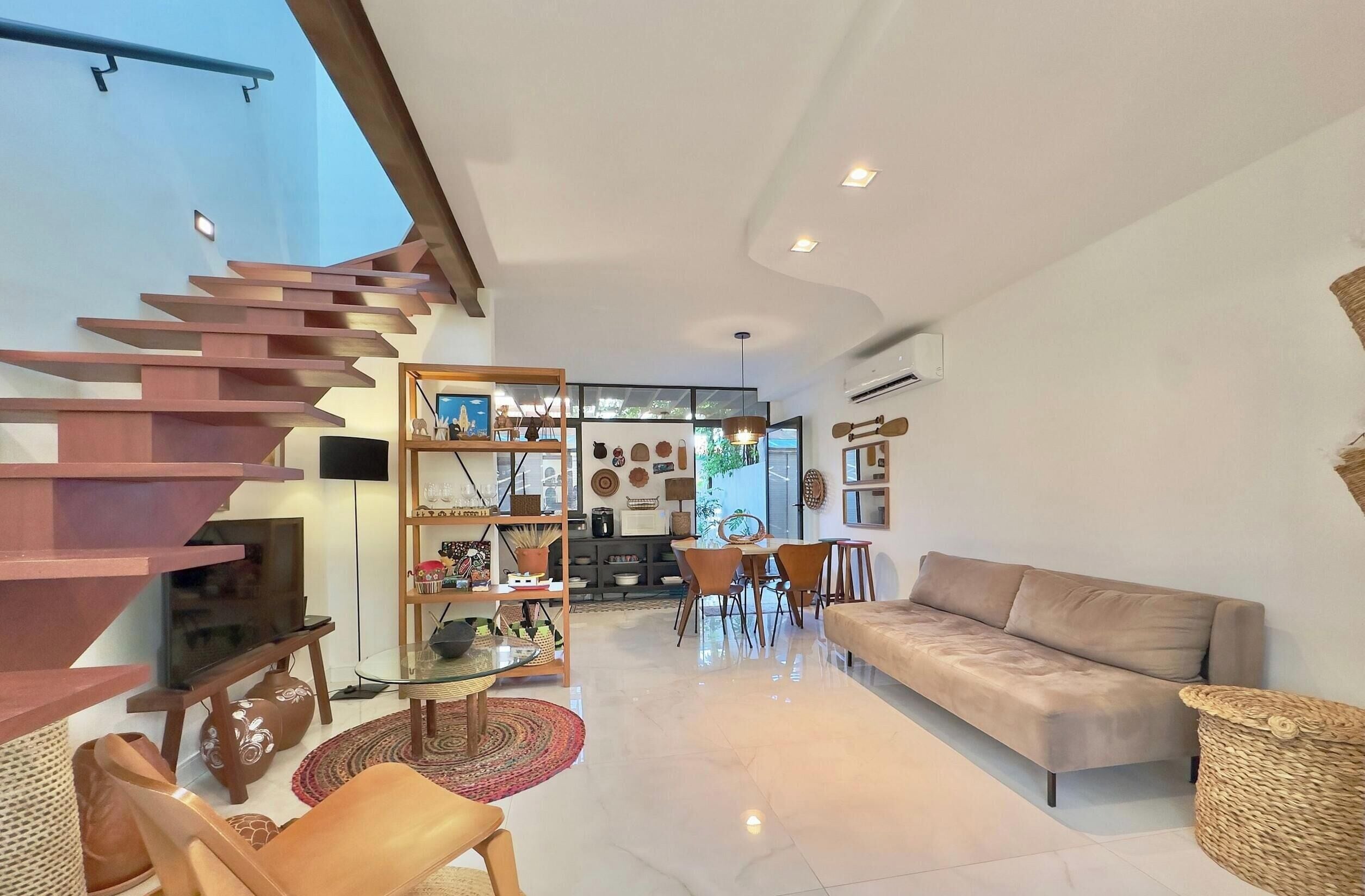 Uma sala de estar moderna com escada, sofá, área de jantar e televisão.