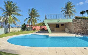 Piscina com muro de pedra, uma espreguiçadeira e um pequeno edifício com varanda.