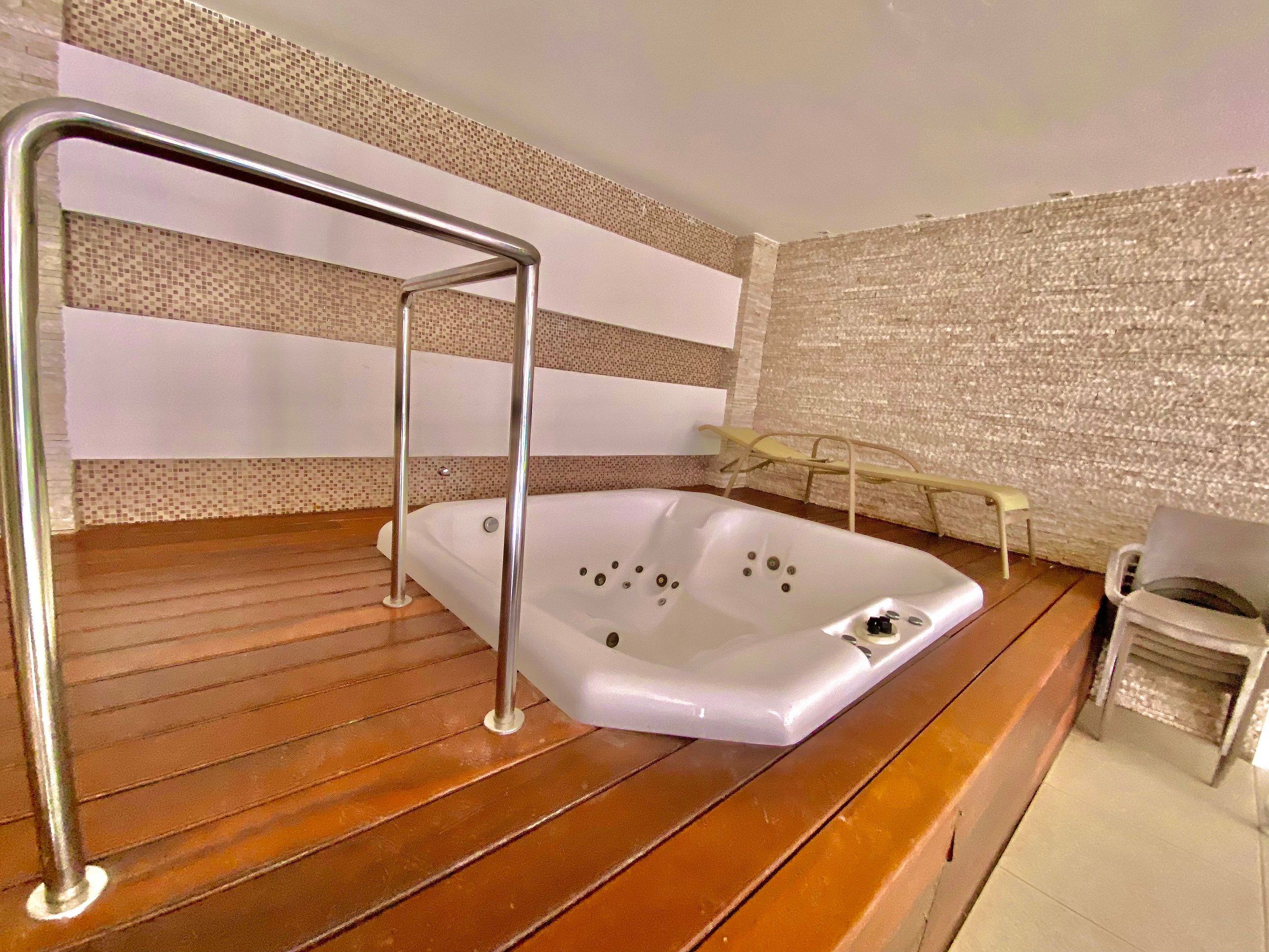 Um quarto de spa com piso de madeira, uma banheira branca e um corrimão de metal.