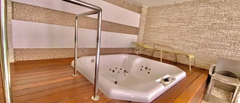 Um quarto de spa com piso de madeira, uma banheira branca e um corrimão de metal.