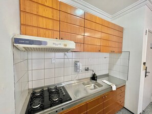 Uma cozinha com fogão a gás, pia, armários de madeira e ar-condicionado fixado na parede.