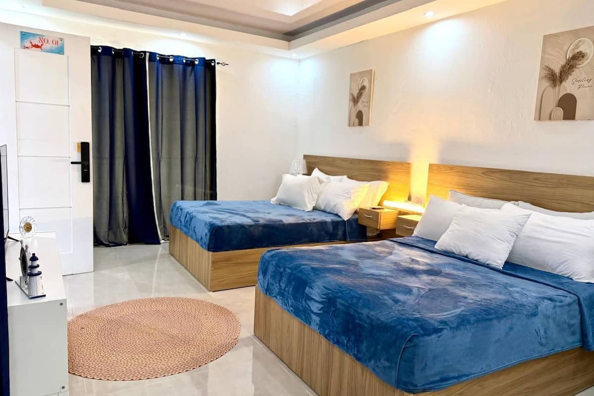 Quarto de hotel com duas camas, uma pequena escrivaninha, uma lâmpada e uma porta com um aviso.