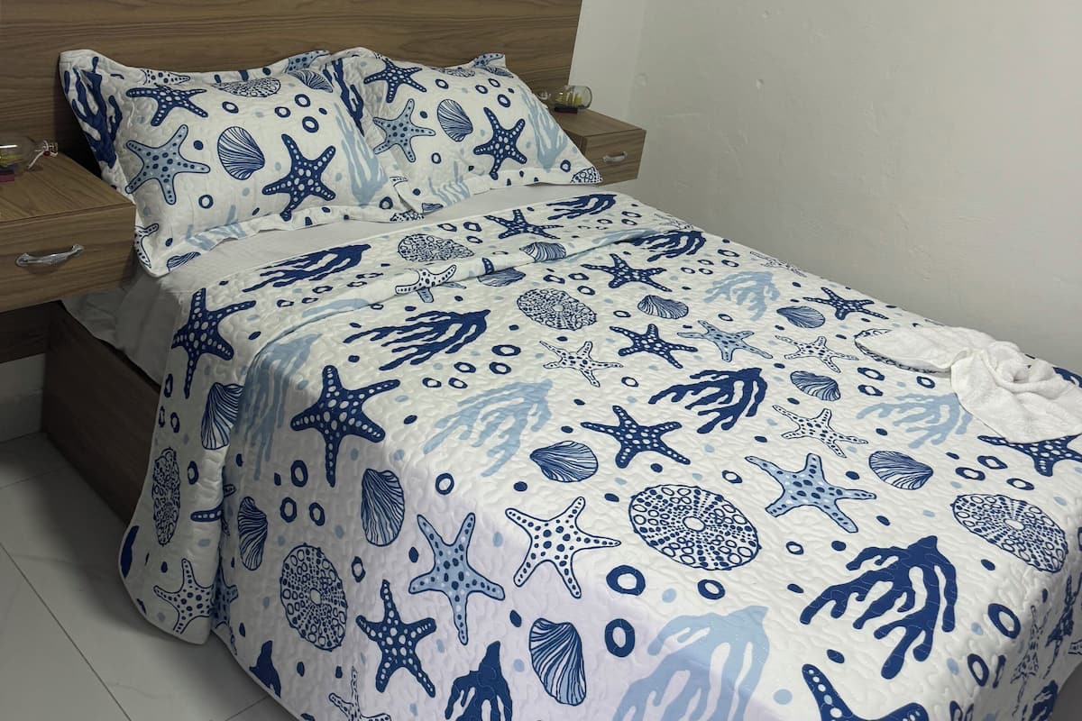 Quarto com cama, cabeceira de madeira, duas mesas de cabeceira, um quadro na parede e decoração com estrelas-do-mar.