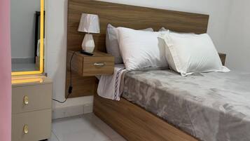 Quarto moderno com cabeceira de madeira, mesa de cabeceira com abajur, espelho e duas pinturas nas paredes.