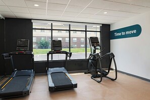 Sala de ginástica com esteiras e uma máquina elíptica, janelas amplas e um letreiro motivacional.