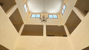 Um átrio amplo com pé direito alto, claraboias, um candelabro e uma coluna de mármore.