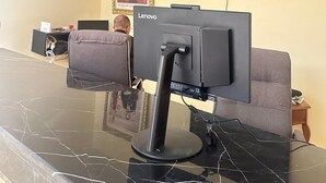 Uma receção com um monitor Lenovo, um retrato emoldurado e uma televisão na parede.