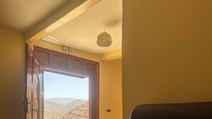 Quarto com sofá de couro, piso ladrilhado, porta que dá para o exterior e luminária pendente.