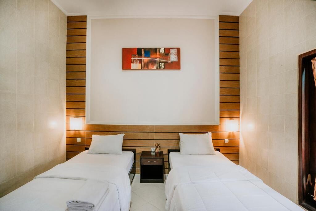 Quarto de hotel com duas camas, cabeceira de madeira, um quadro na parede e duas luminárias de apoio.
