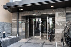 Entrada de um edifício com porta de vidro, uma placa com o nome 'REBANGA' e uma motocicleta estacionada na frente.