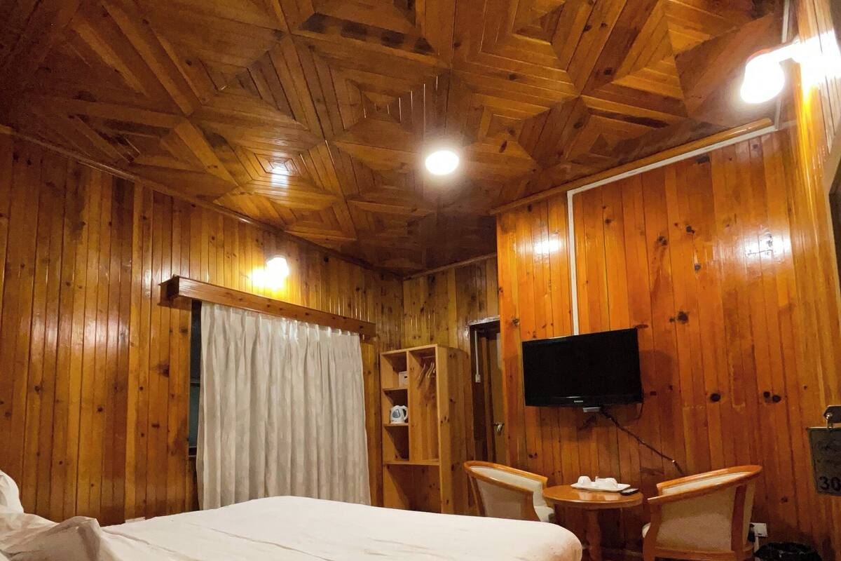 Quarto com painéis de madeira, uma cama, uma escrivaninha, uma cadeira e uma televisão.