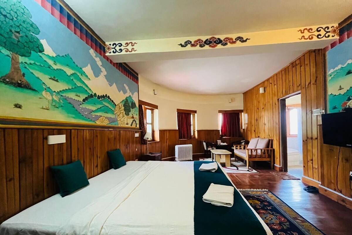 Quarto de hotel com uma cama grande, uma escrivaninha, uma cadeira, uma televisão e um mural na parede.