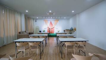 Uma sala de conferências com mesas e cadeiras, um palco com cortinas e uma planta ao lado.