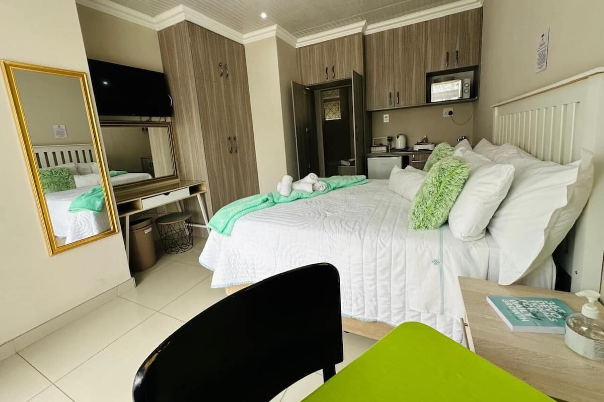 Quarto com cama, mesa de cabeceira, espelho e escrivaninha com cadeira.