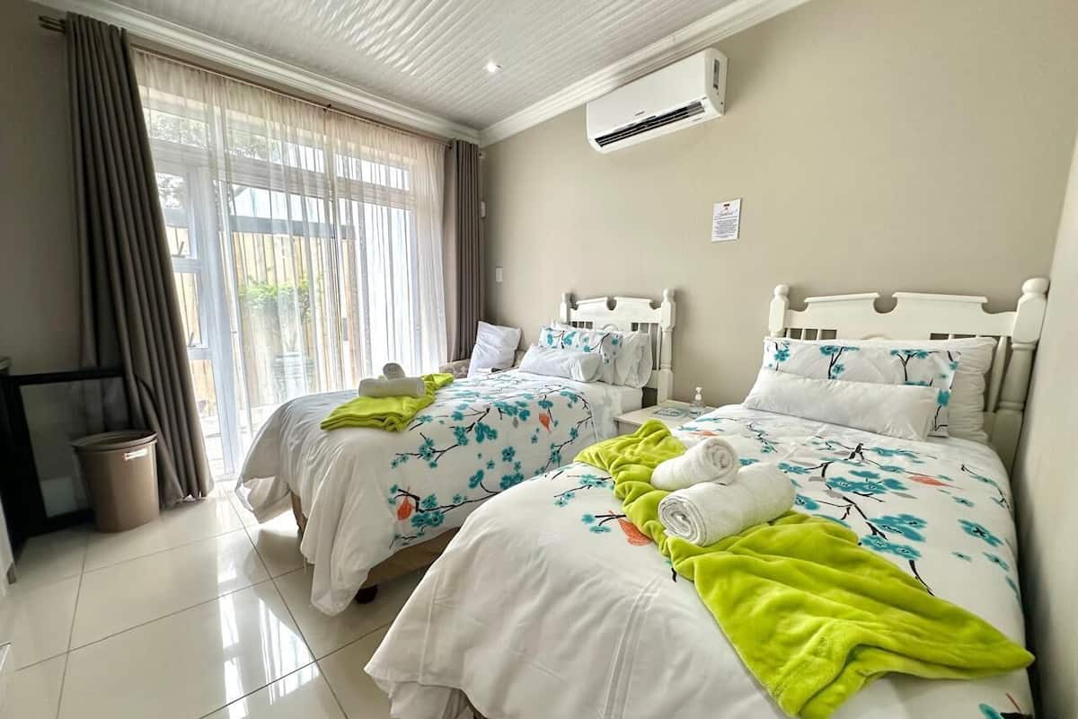 Quarto de hotel com duas camas, uma lixeira, um ar condicionado e uma janela com cortinas.