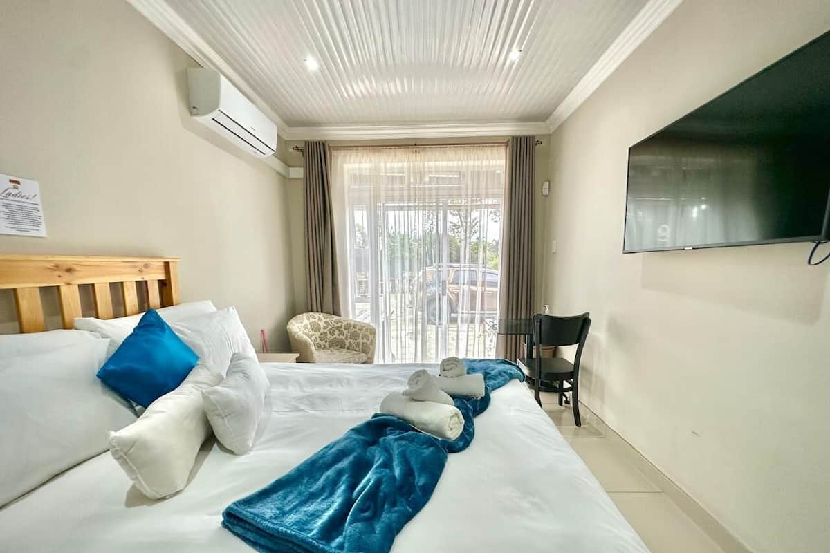 Quarto de hotel com duas camas, televisão, uma cadeira e varanda com vista.