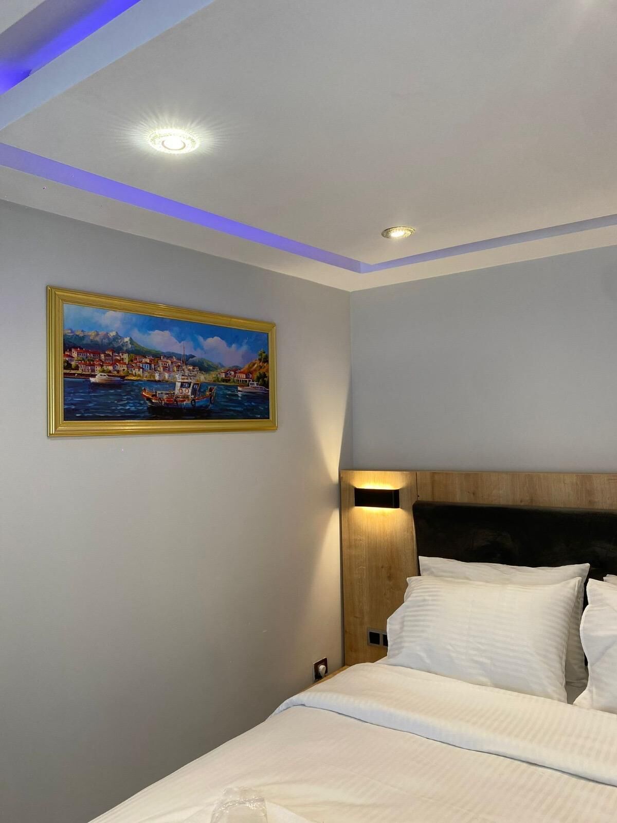 Quarto de hotel com cama, pintura de uma paisagem costeira e luminária no teto.