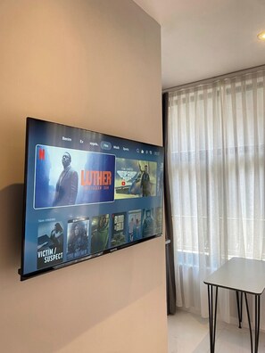 Televisão de tela plana presa na parede exibindo uma interface de serviço de streaming com diversas opções de filmes.