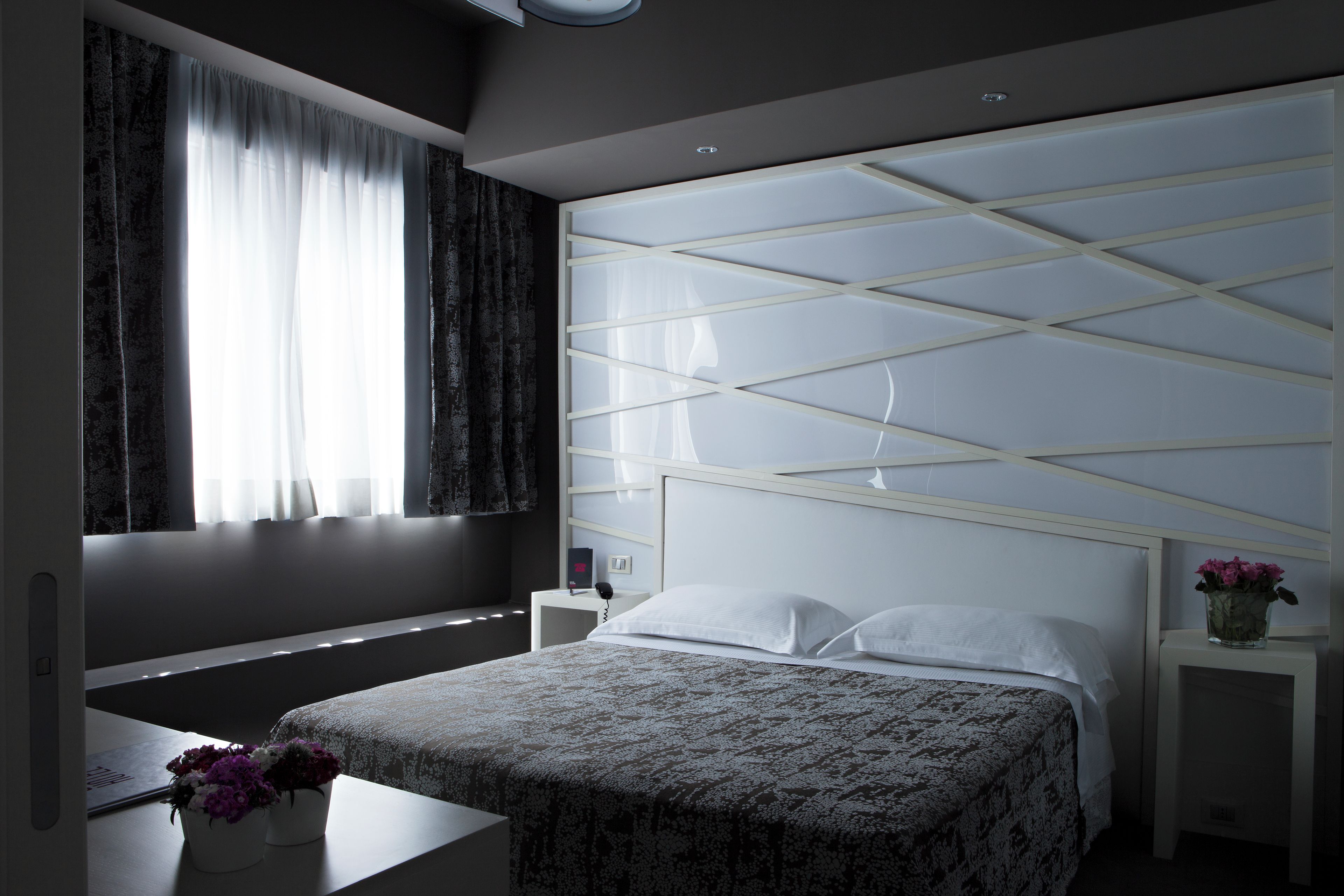 Um quarto moderno com uma cama, mesas de cabeceira e uma janela com cortinas.