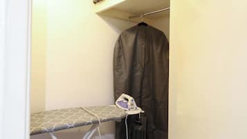 Quarto compacto com tábua de passar roupa fixada na parede, uma peça de roupa pendurada e uma pequena prateleira acima da tábua.