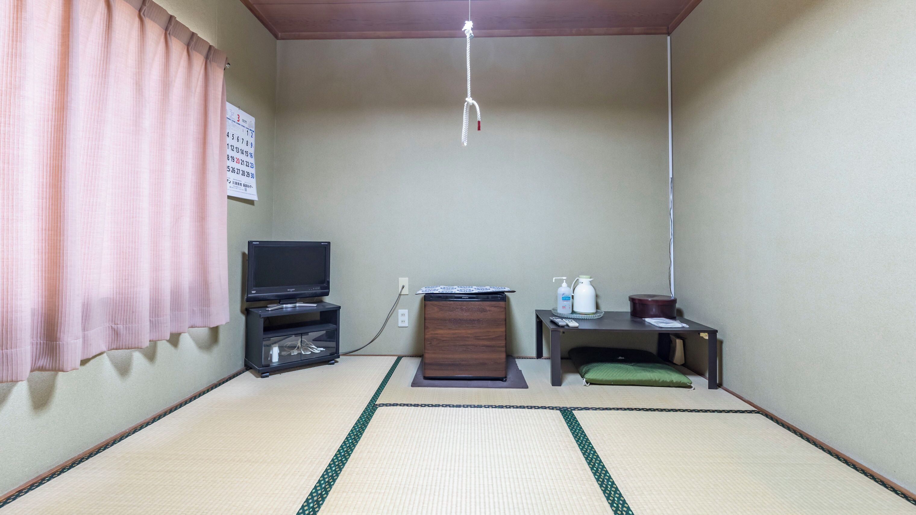 Quarto com tatames, uma televisão, um pequeno armário, um controle remoto e um calendário na parede.