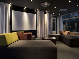 Uma sala de estar moderna com uma televisão de tela plana grande, assentos confortáveis e vista para a cidade à noite.