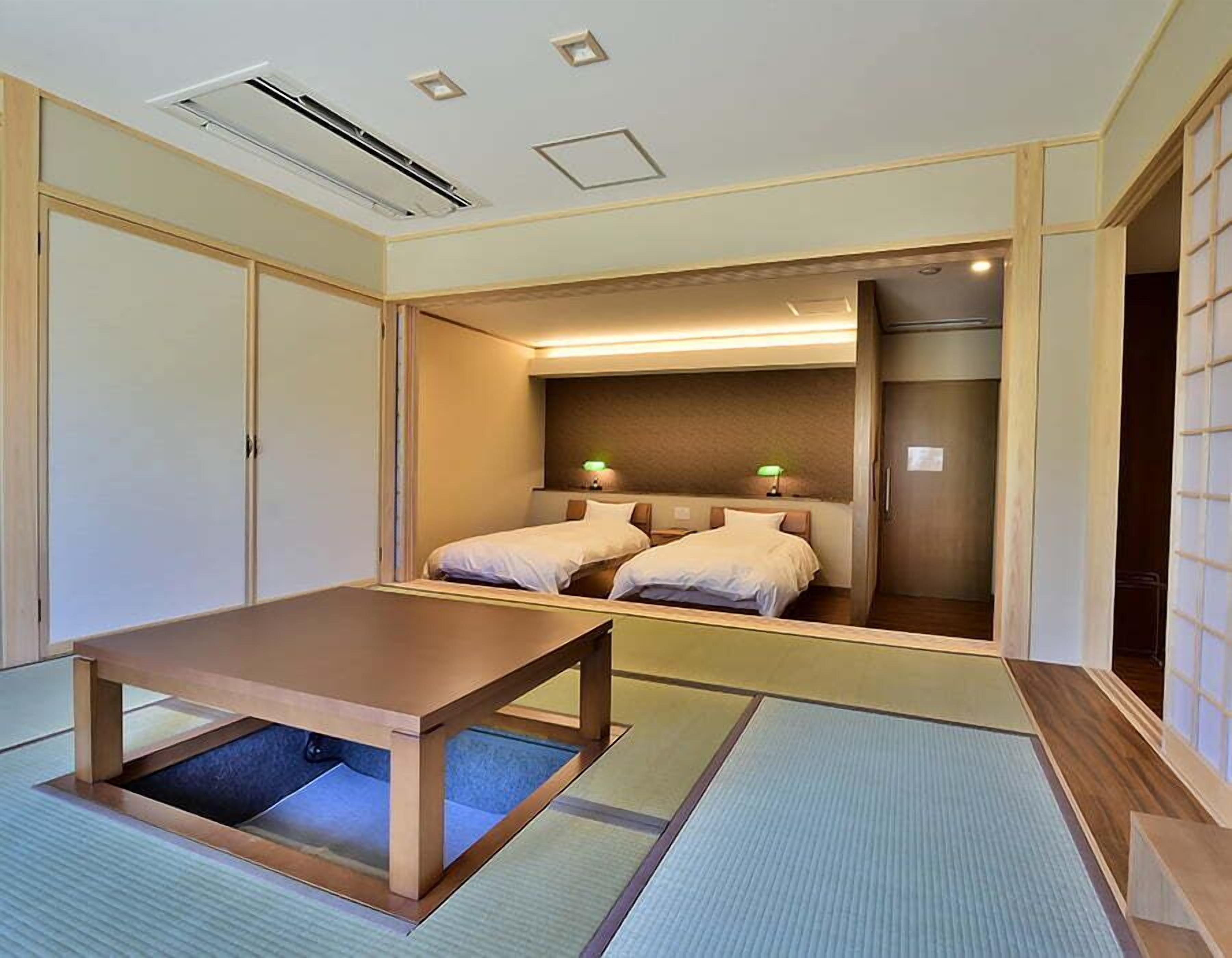 Quarto em estilo japonês tradicional com tatames, uma mesa de madeira baixa, duas camas com almofadas e uma porta deslizante.