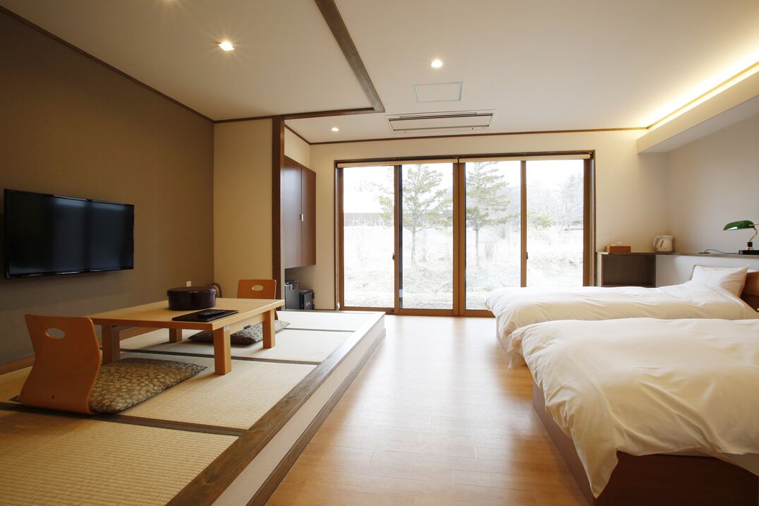 Quarto de hotel moderno com uma cama, uma escrivaninha, televisão e porta de correr para uma varanda.
