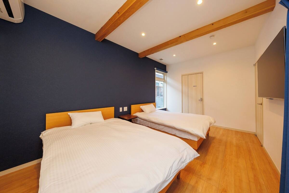 Quarto com duas camas, vigas de madeira no teto, uma janela e uma porta.