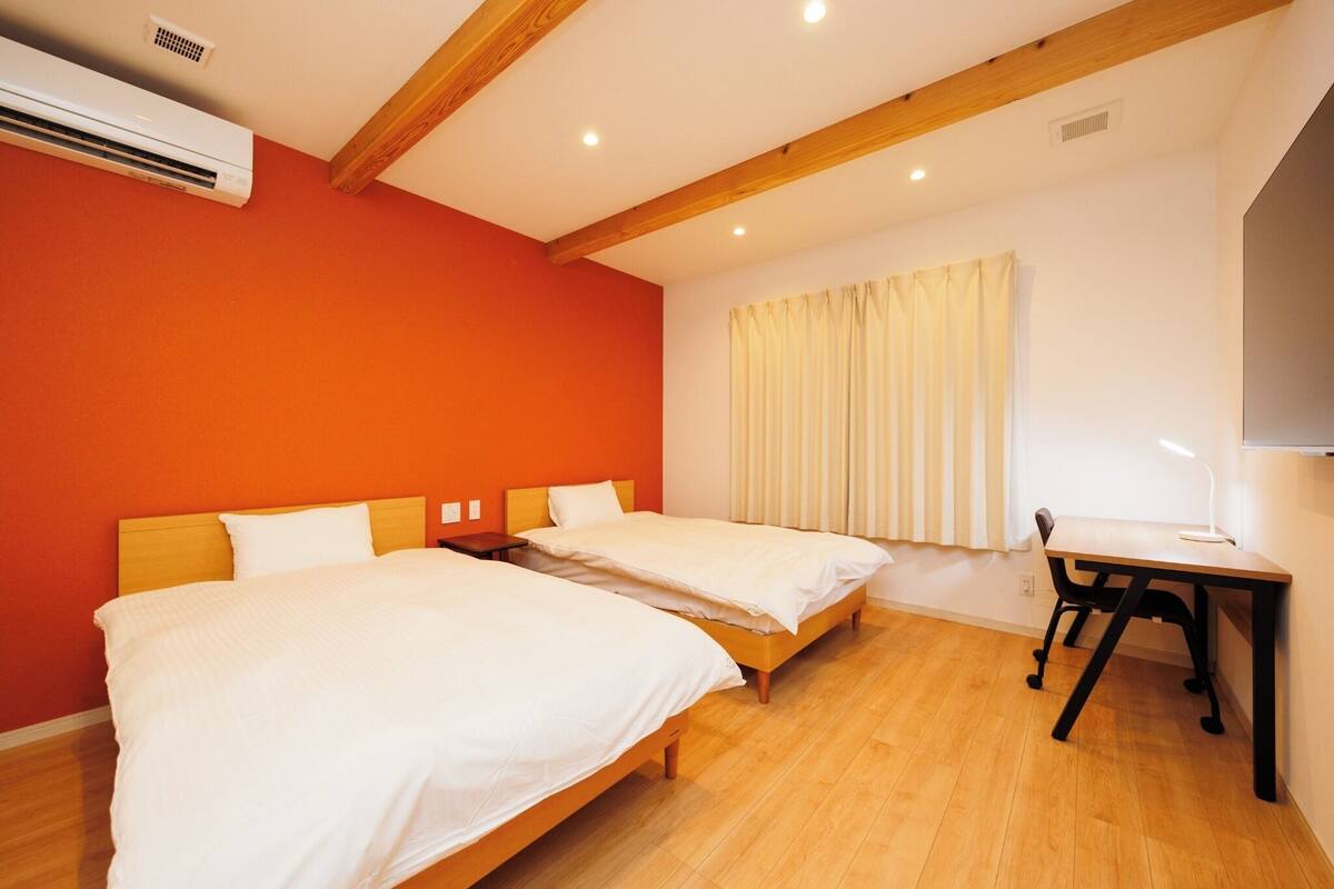 Quarto de hotel com duas camas, uma escrivaninha e aparelho de ar condicionado.