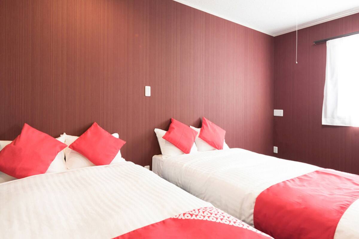 Quarto de hotel com duas camas, roupa de cama vermelha e branca, e uma parede de madeira.