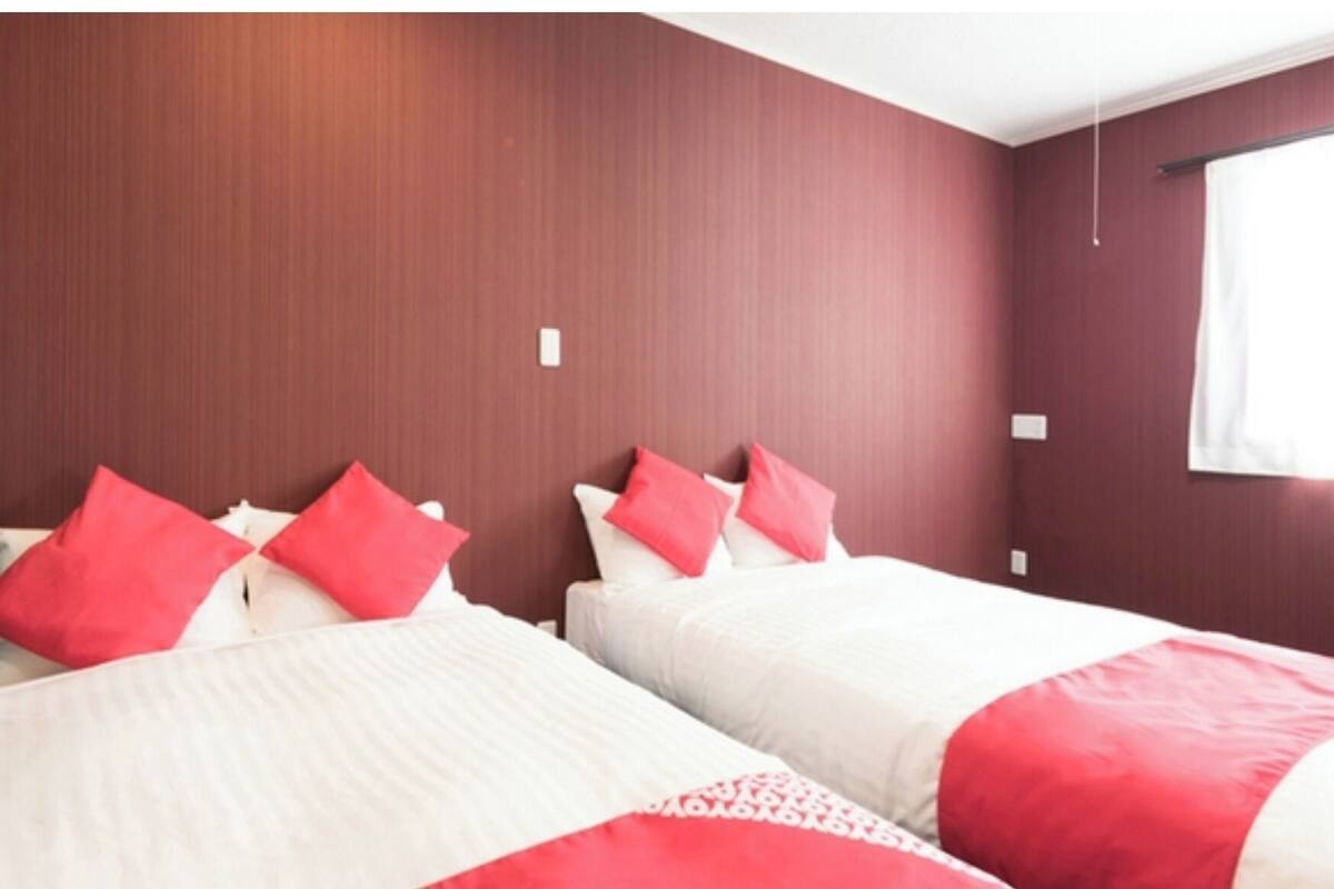 Quarto de hotel com duas camas, cada uma com roupa de cama vermelha e branca, e uma parede de madeira.