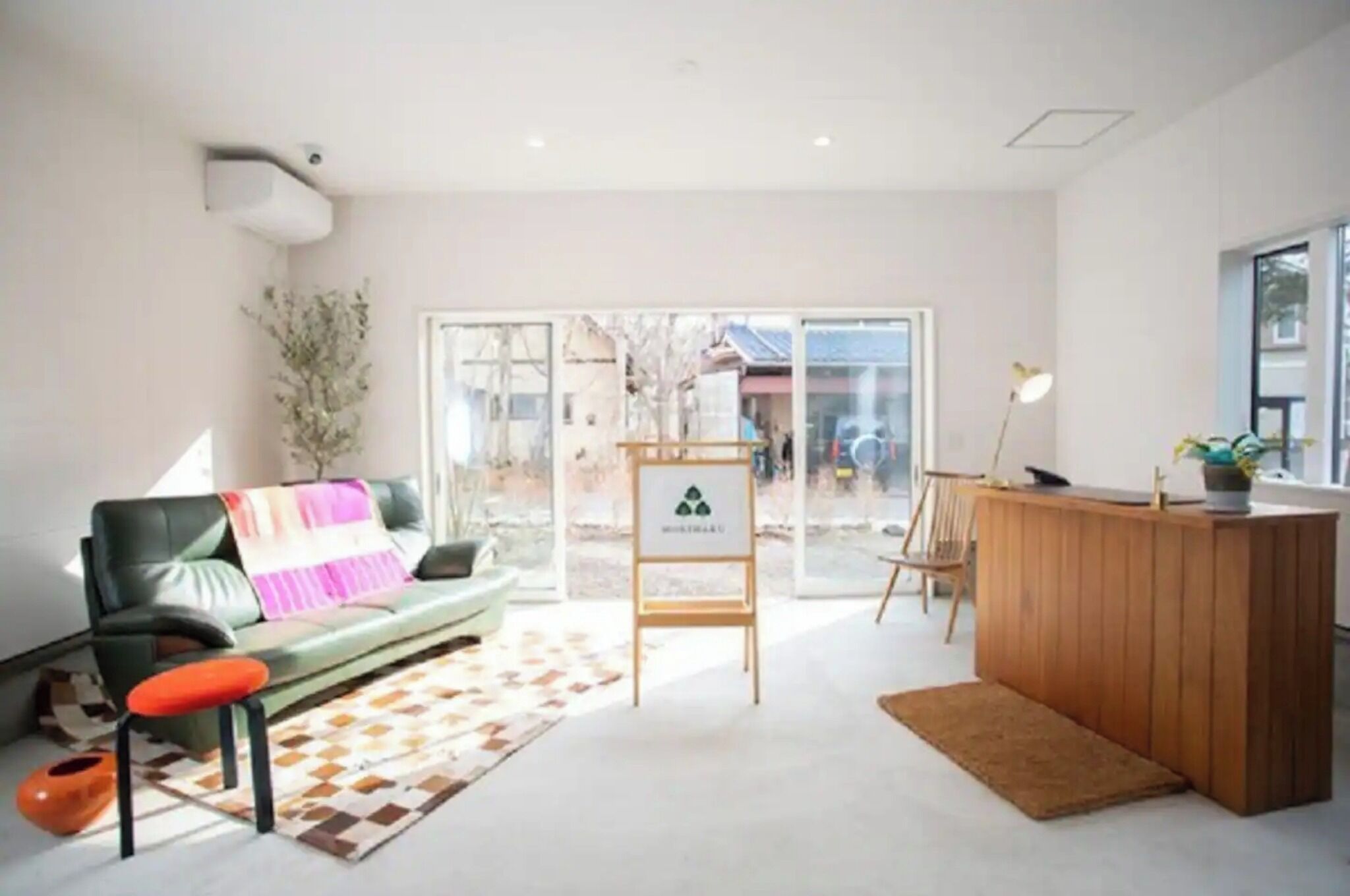 Um interior moderno com um sofá, um balcão de recepção de madeira e uma grande porta de vidro que dá para o exterior.