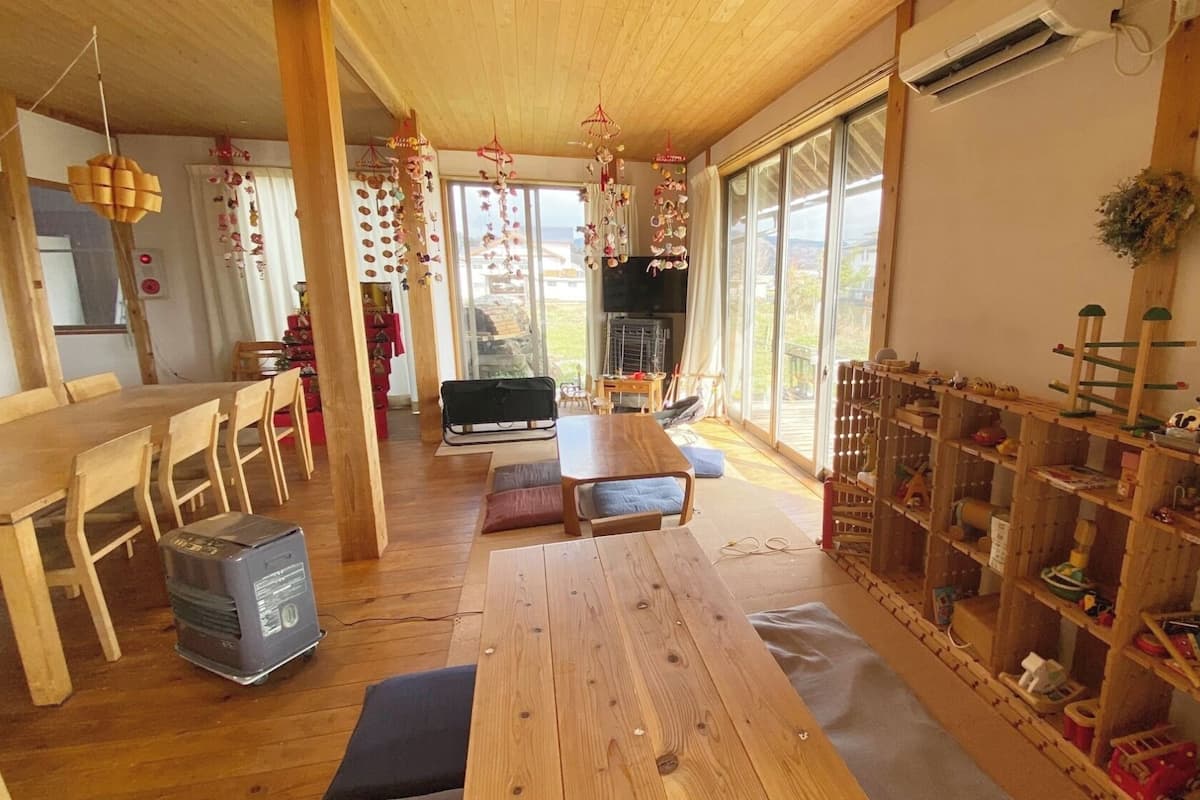 Um quarto espaçoso com uma mesa de jantar de madeira, cadeiras, um sofá e uma estante cheia de brinquedos.