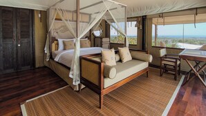 Cama com dossel e cortina, vista para a paisagem, uma escrivaninha de madeira e uma cadeira.