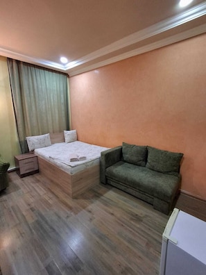 Quarto com uma cama, um sofá verde, uma mesa de cabeceira e uma pequena mesa.