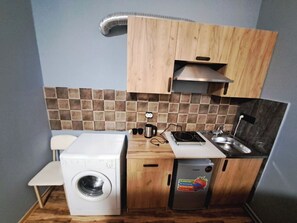 Uma cozinha compacta com máquina de lavar, pequena geladeira, pia e armários de madeira.