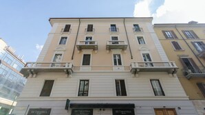 Um edifício de vários andares com varandas, um restaurante no térreo e uma placa indicando '101 Tarantella Milano'.