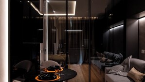 Quarto de hotel moderno com área de refeições, um sofá e uma divisória de vidro.