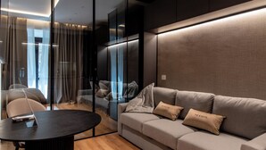 Quarto de hotel moderno com sofá, divisória de vidro, mesa redonda e vista para o exterior.